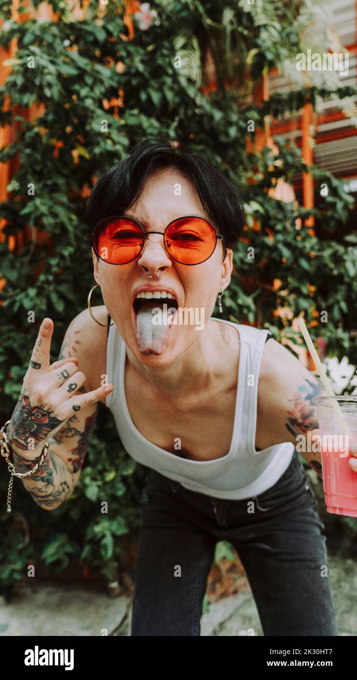 Hipster woman sticking out tongue gesturing horn sign Stock Photo - Alamy
