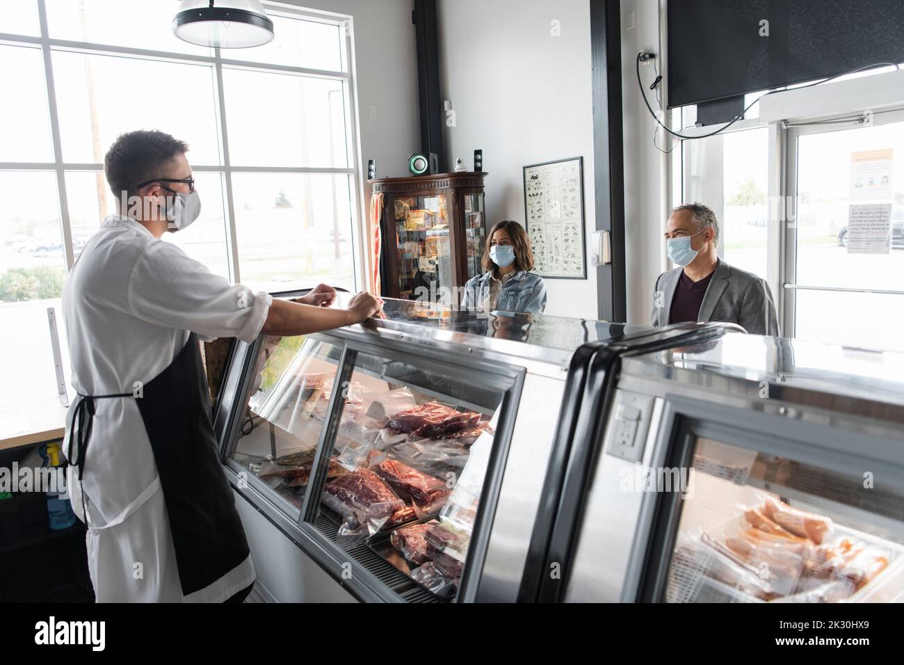 Butcher wearing face mask serving couple in shop Stock Photo - Alamy