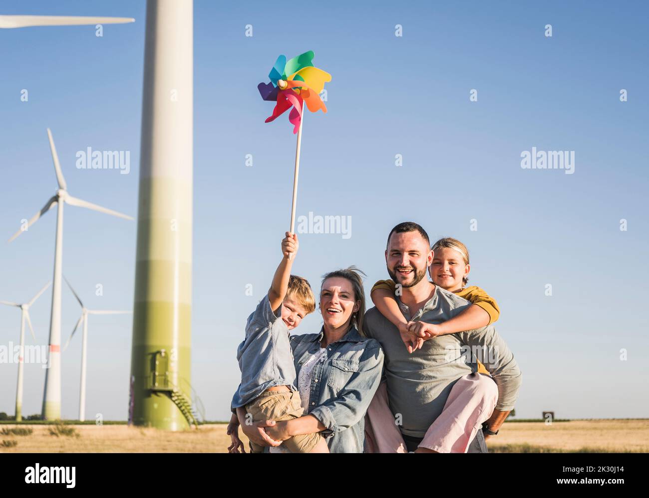 Optimistic family standing in wind park son carrying colorful pinwheel ...