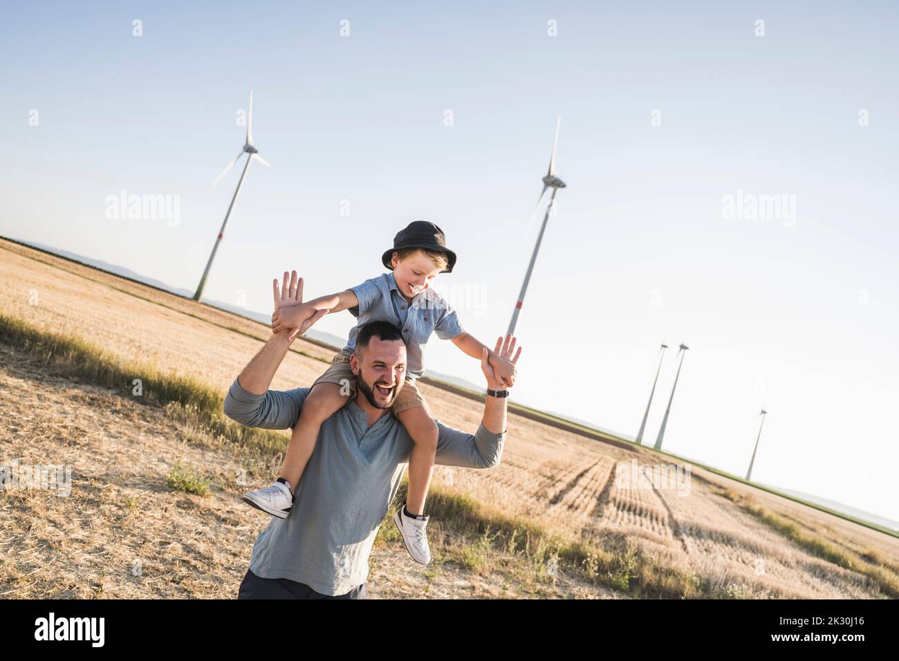 Father carrying son on shoulders in front of wind turbines Stock Photo ...