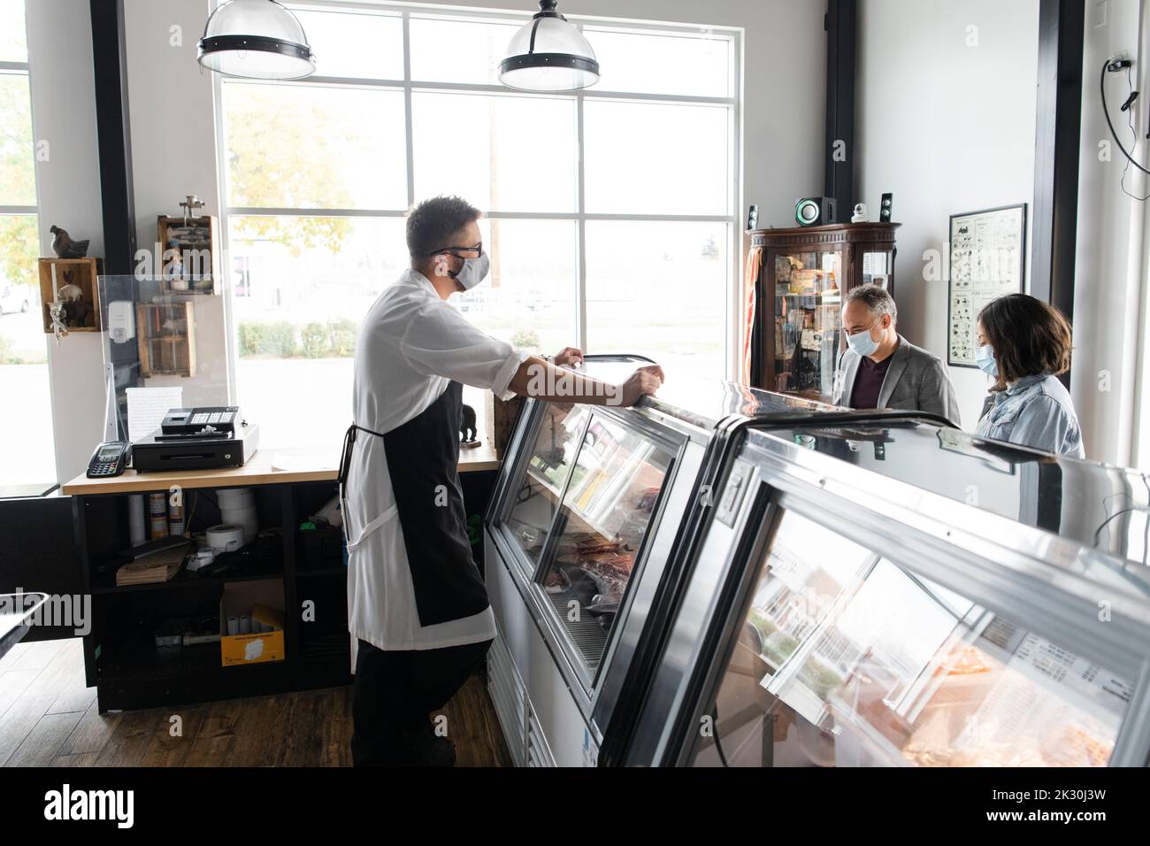 Butcher wearing face mask serving couple in shop Stock Photo - Alamy