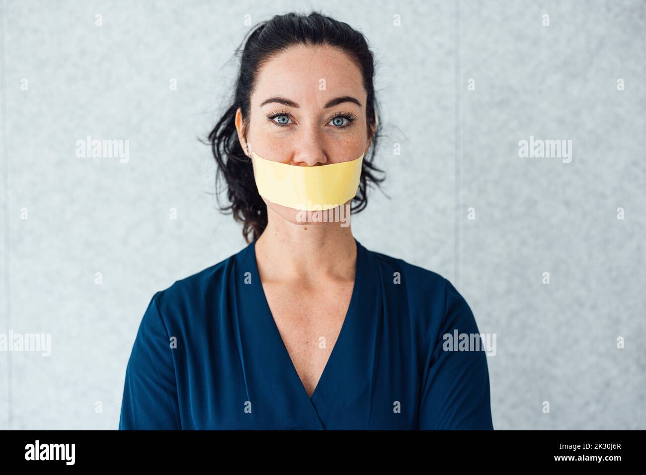 Woman with tape over mouth standing in front of gray wall Stock Photo ...