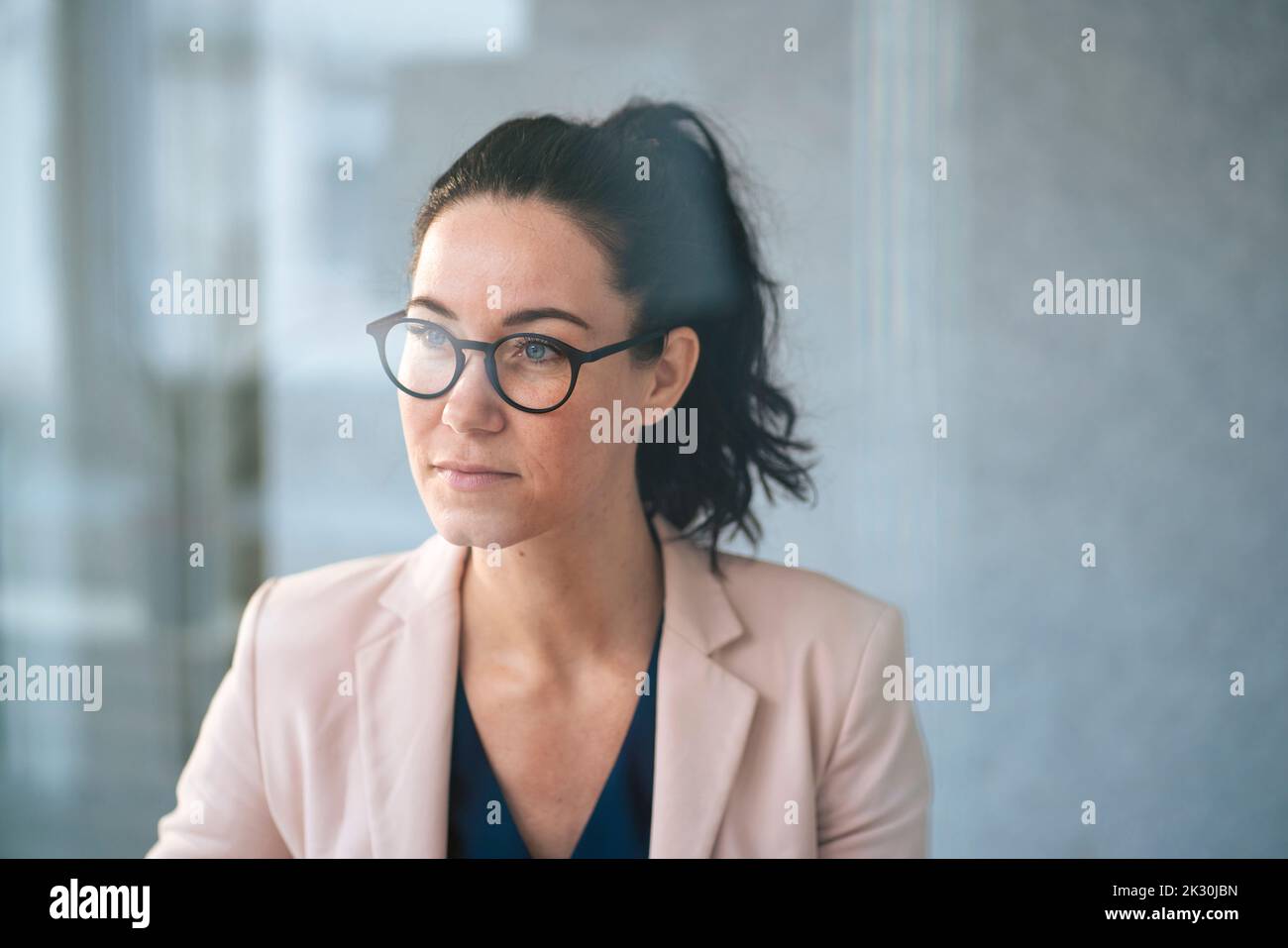 Thoughtful businesswoman wearing eyeglasses in front of wall seen ...