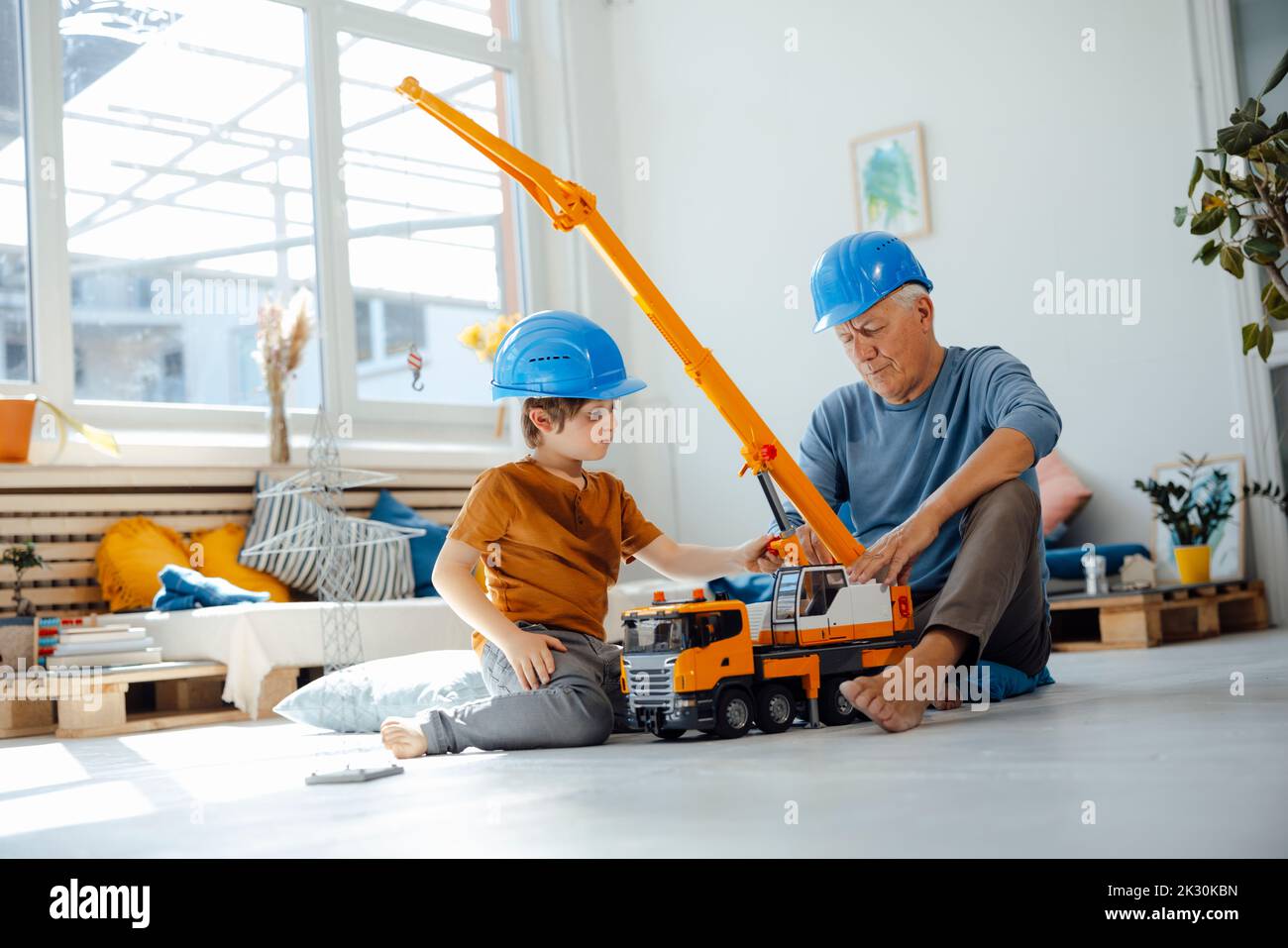 Boy playing with crane toy by grandfather in living room Stock Photo ...