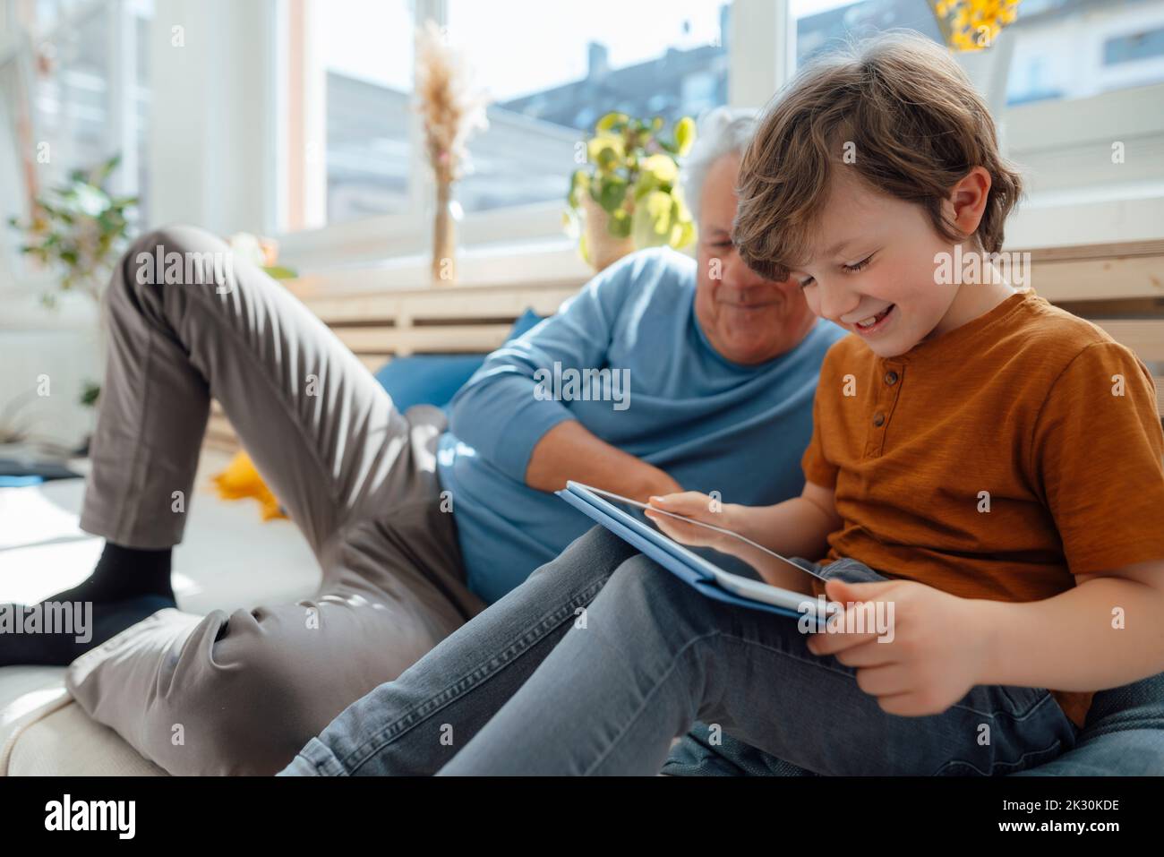 Happy grandson using tablet PC by grandfather in living room Stock ...