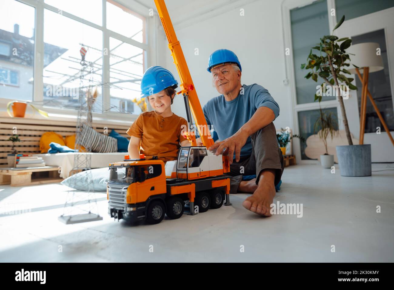 Smiling grandson and grandfather in hardhats with toy crane and ...