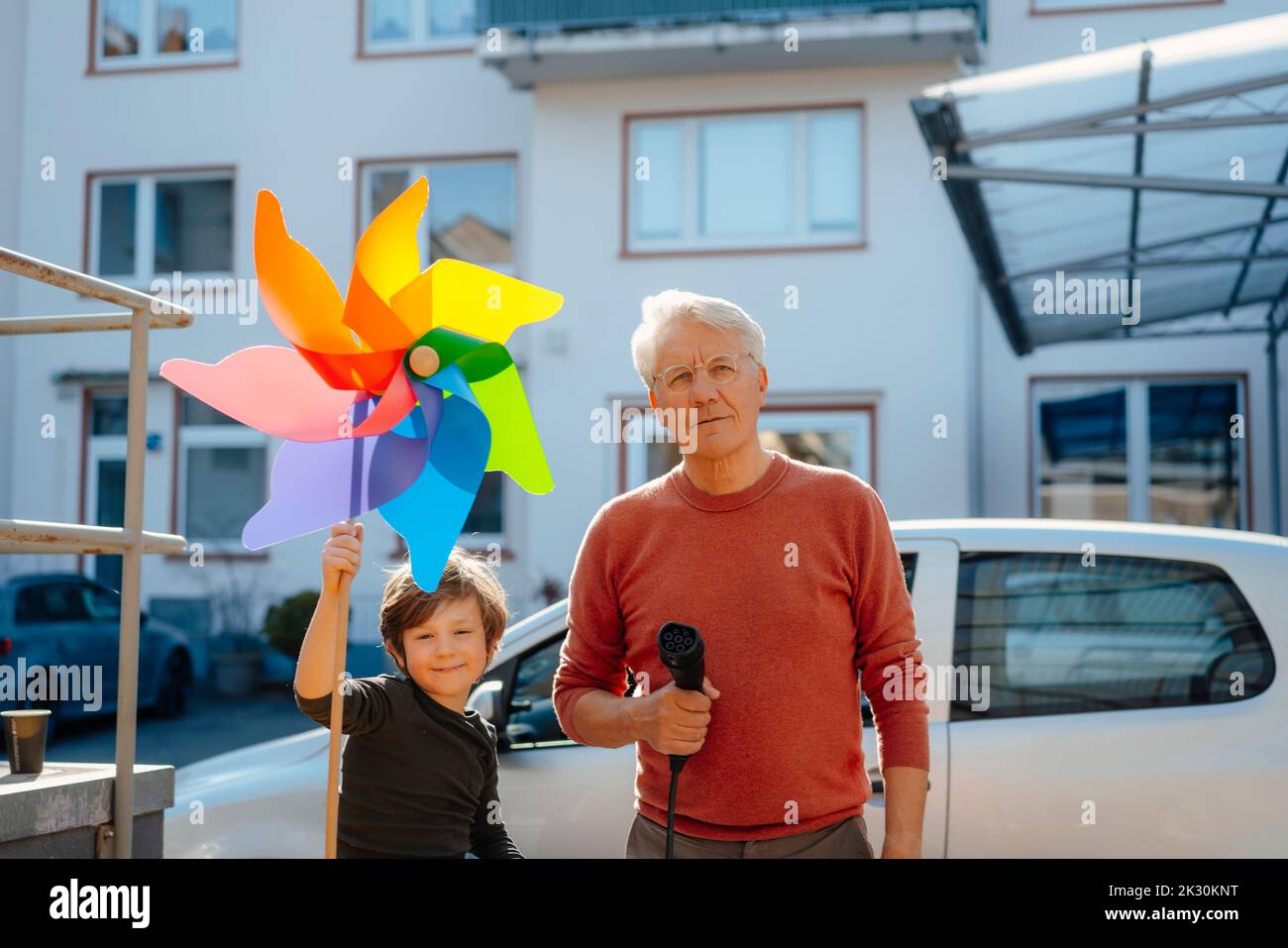Smiling boy holding pinwheel toy by grandfather with charging plug ...