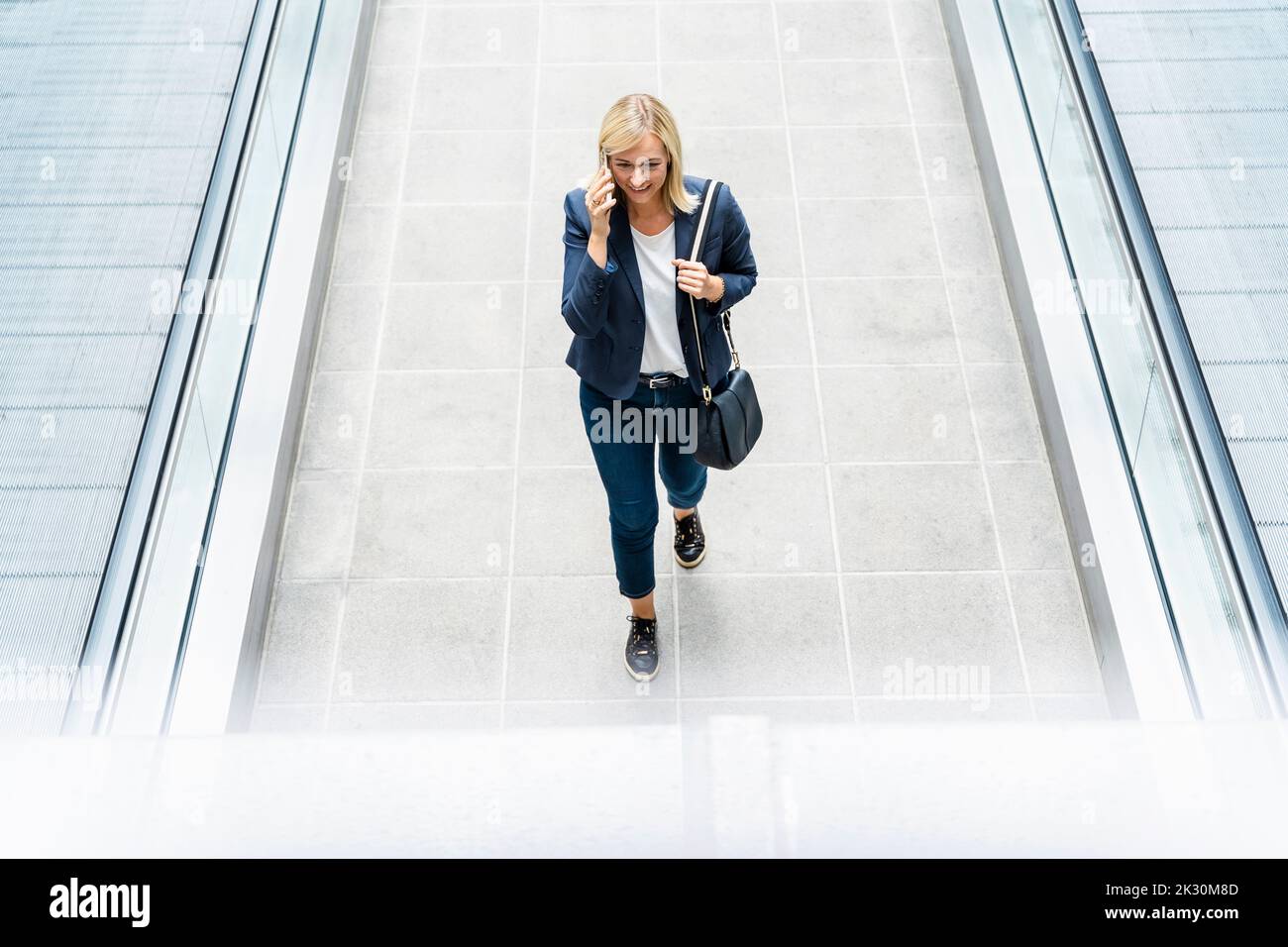 Businesswoman talking over phone walking on walkway Stock Photo - Alamy
