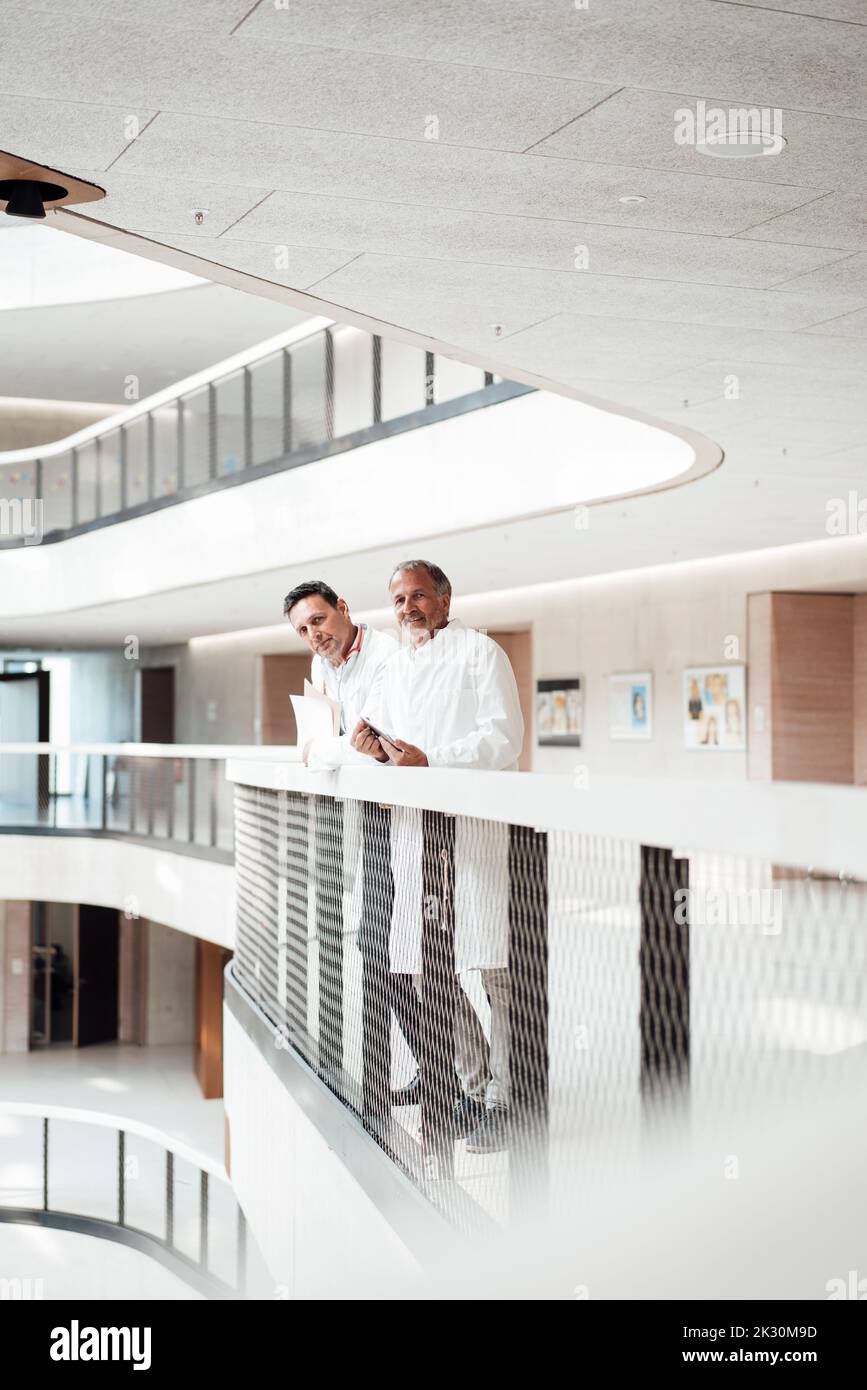 Smiling doctors standing near railing in hospital corridor Stock Photo ...