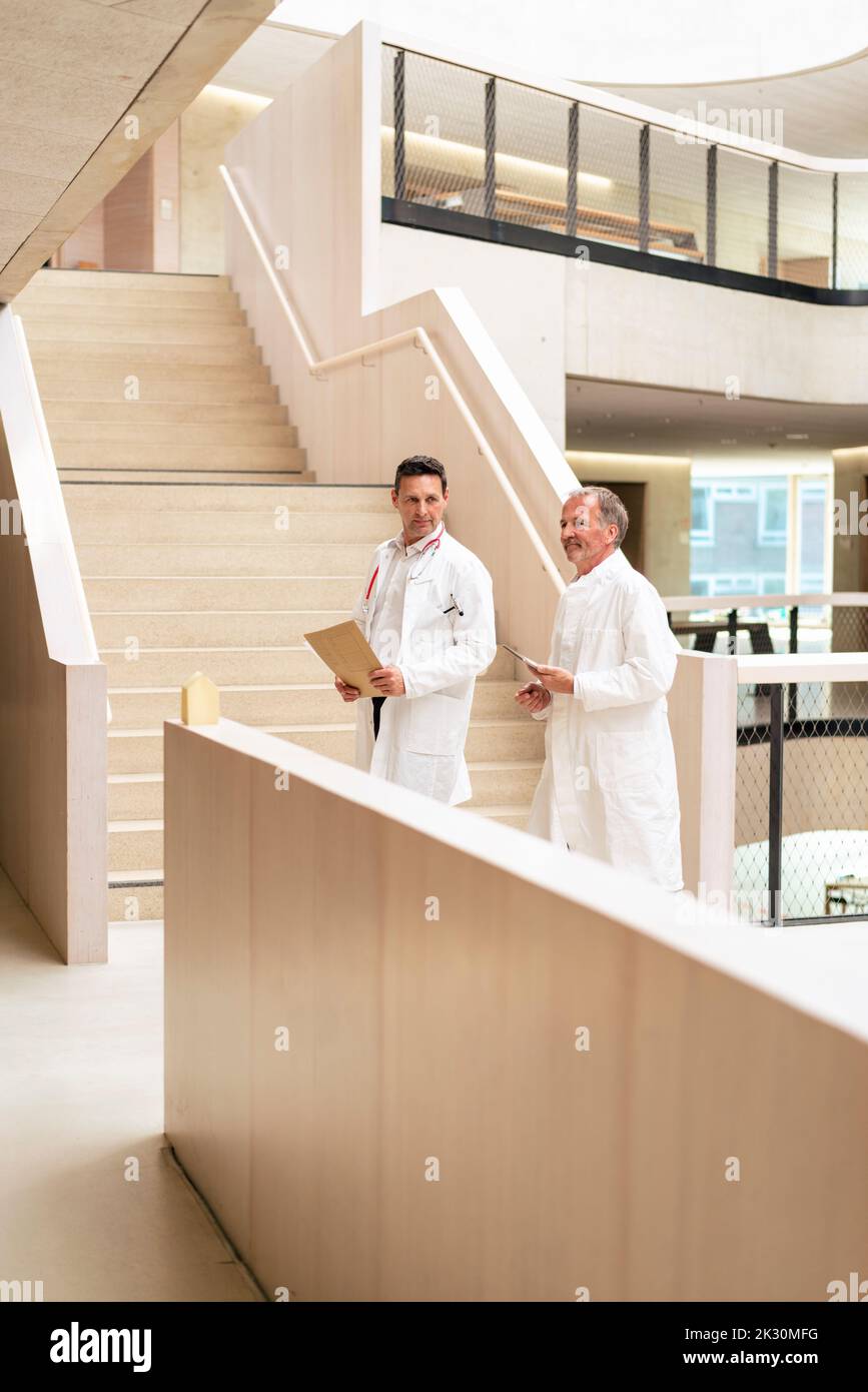 Doctors walking in corridor by railing at hospital Stock Photo - Alamy