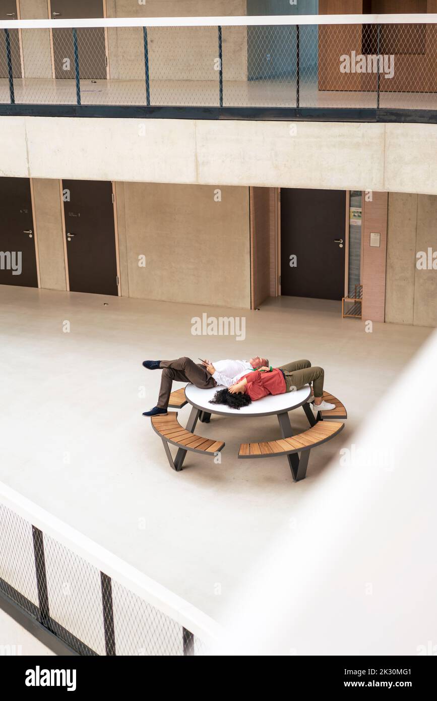 Business colleagues relaxing lying down on table in office lobby Stock ...