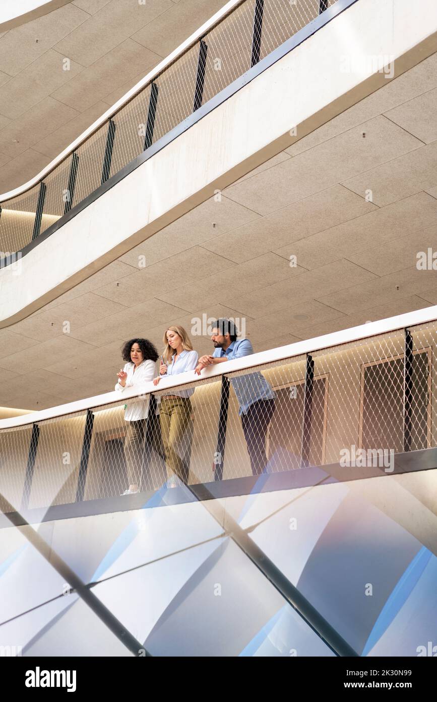 Multiracial business people leaning on railing in corridor Stock Photo ...