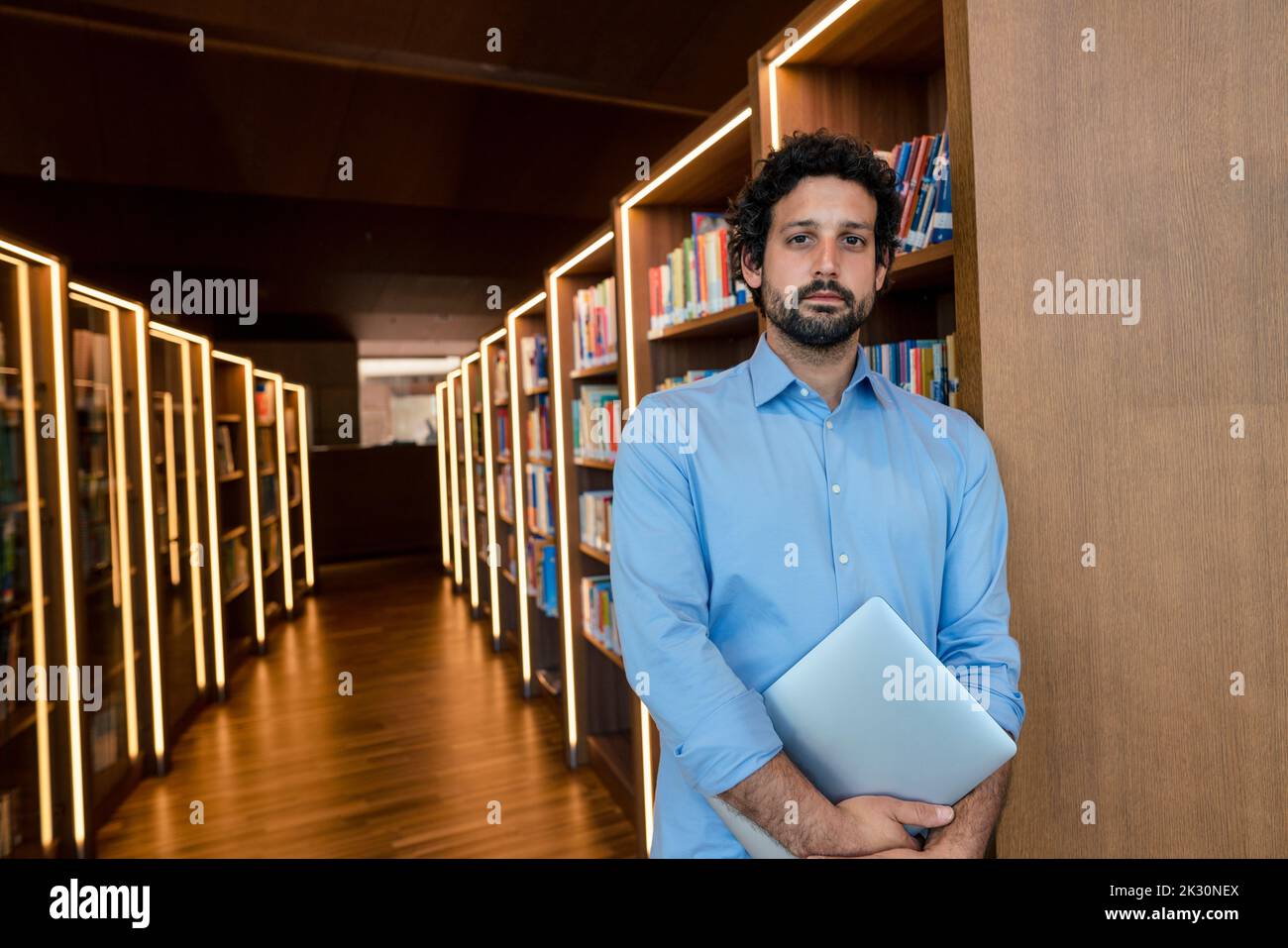 Man with laptop by bookshelf in library Stock Photo - Alamy