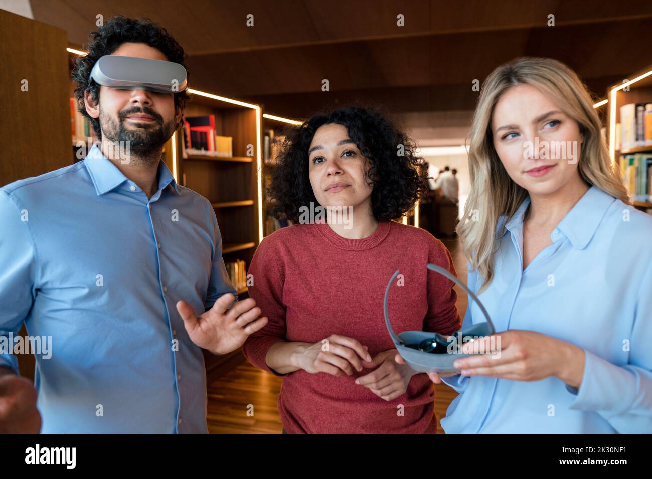 Man watching through VR glasses by colleagues in library Stock Photo ...
