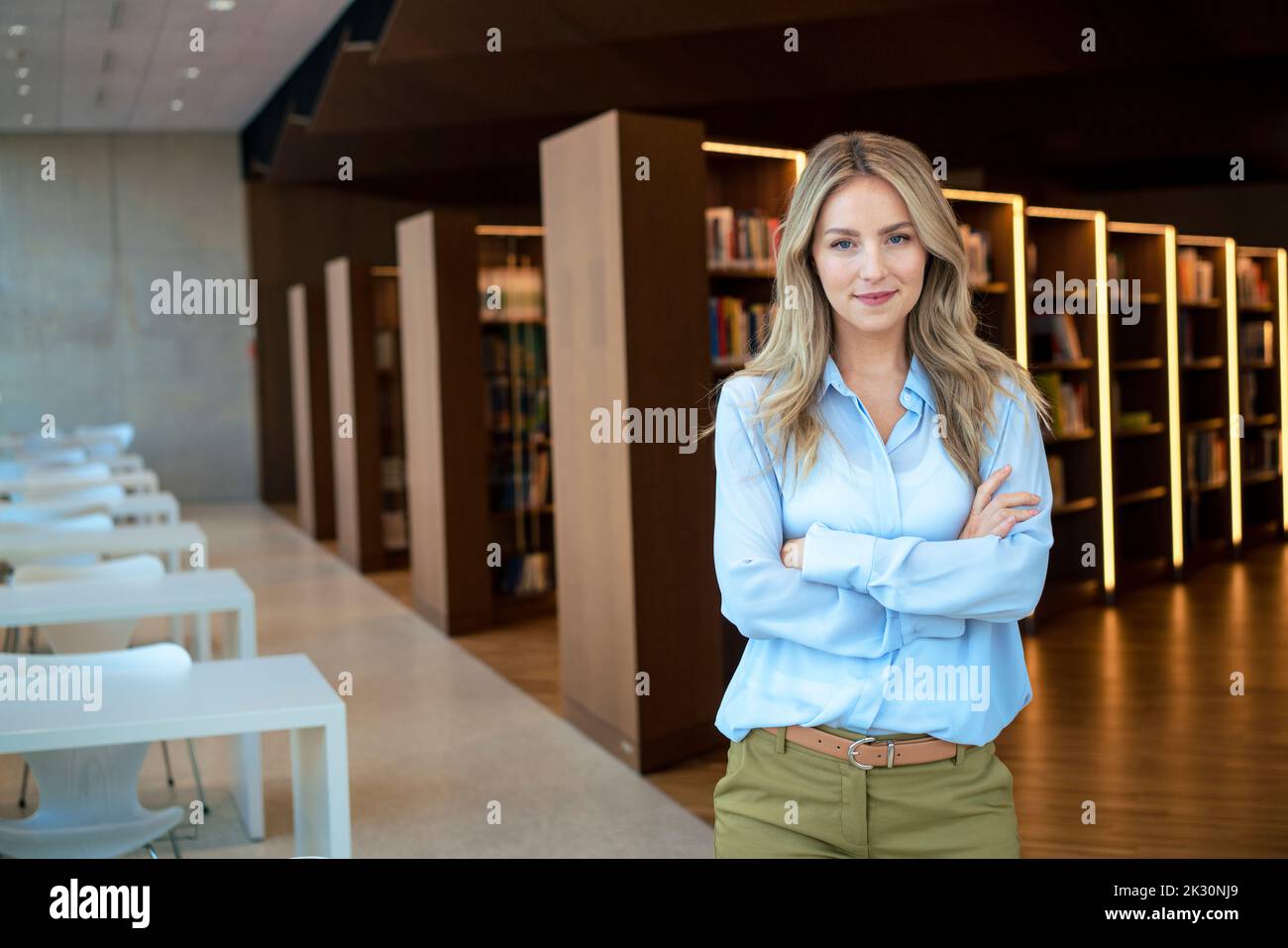 Confident woman in smart casual with arms crossed at illuminated ...