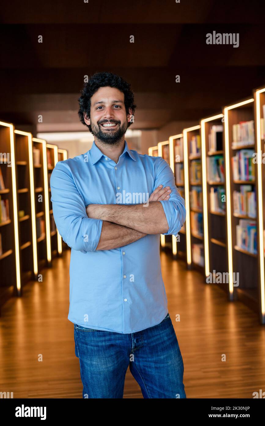 Happy man with arms crossed in illuminated library Stock Photo - Alamy