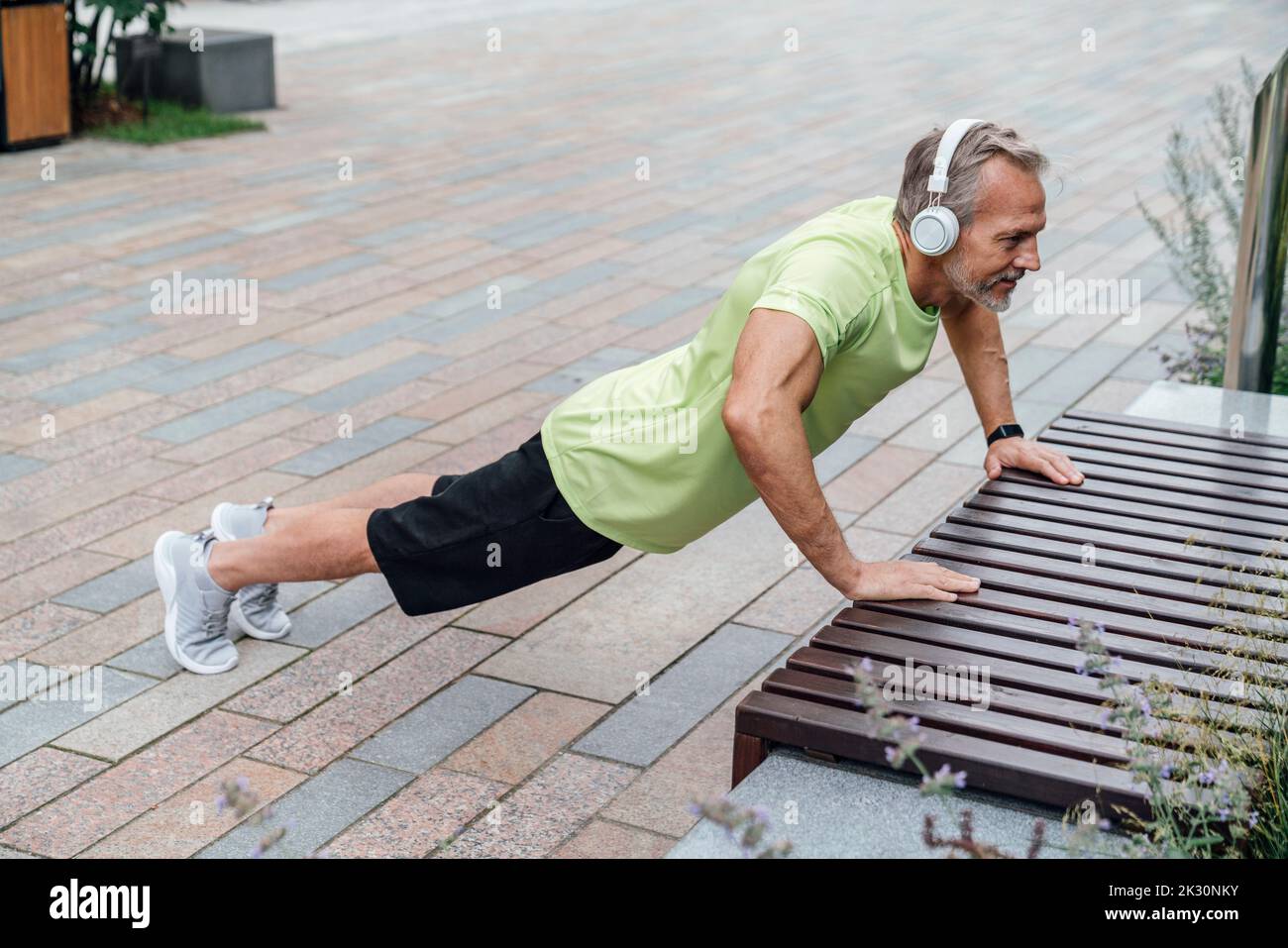 Man wearing wireless headphones doing push-ups on bench Stock Photo - Alamy