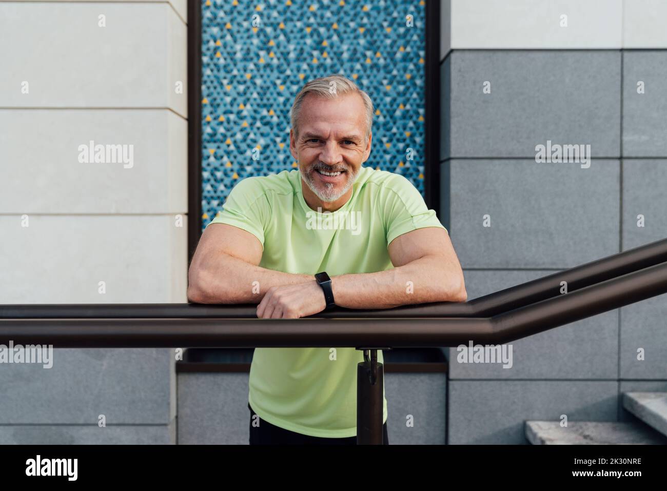 Smiling mature man leaning on metal railing Stock Photo - Alamy
