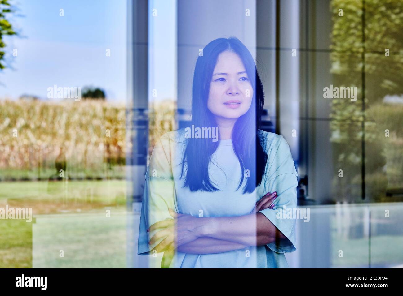 Mature woman standing with arms crossed seen through glass Stock Photo ...