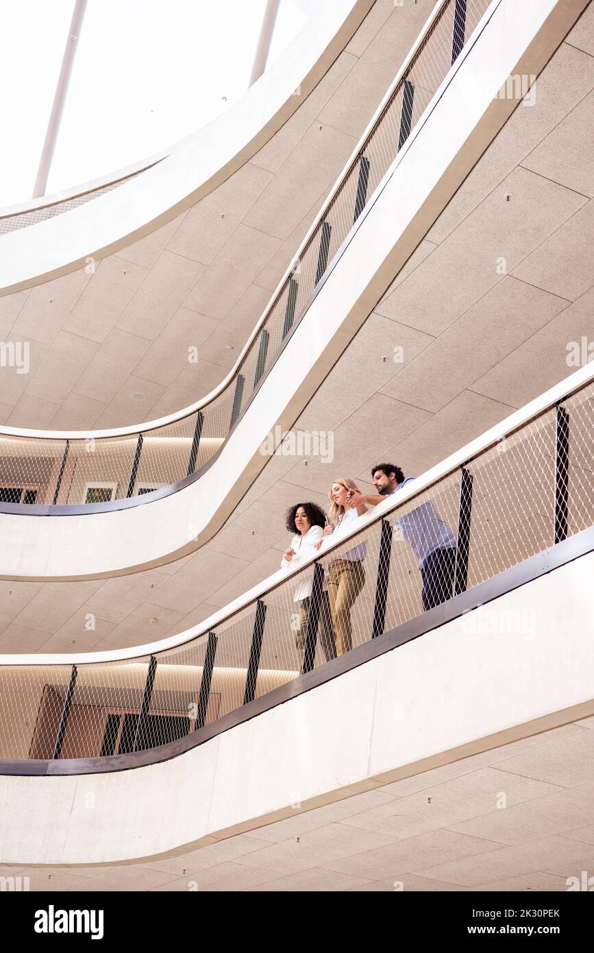 Multiracial business colleagues leaning on railing in corridor Stock ...