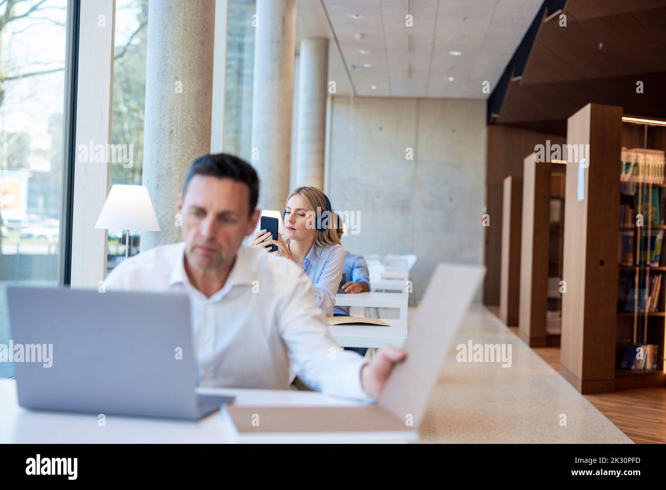 Mature professor working on laptop at desk in library Stock Photo - Alamy