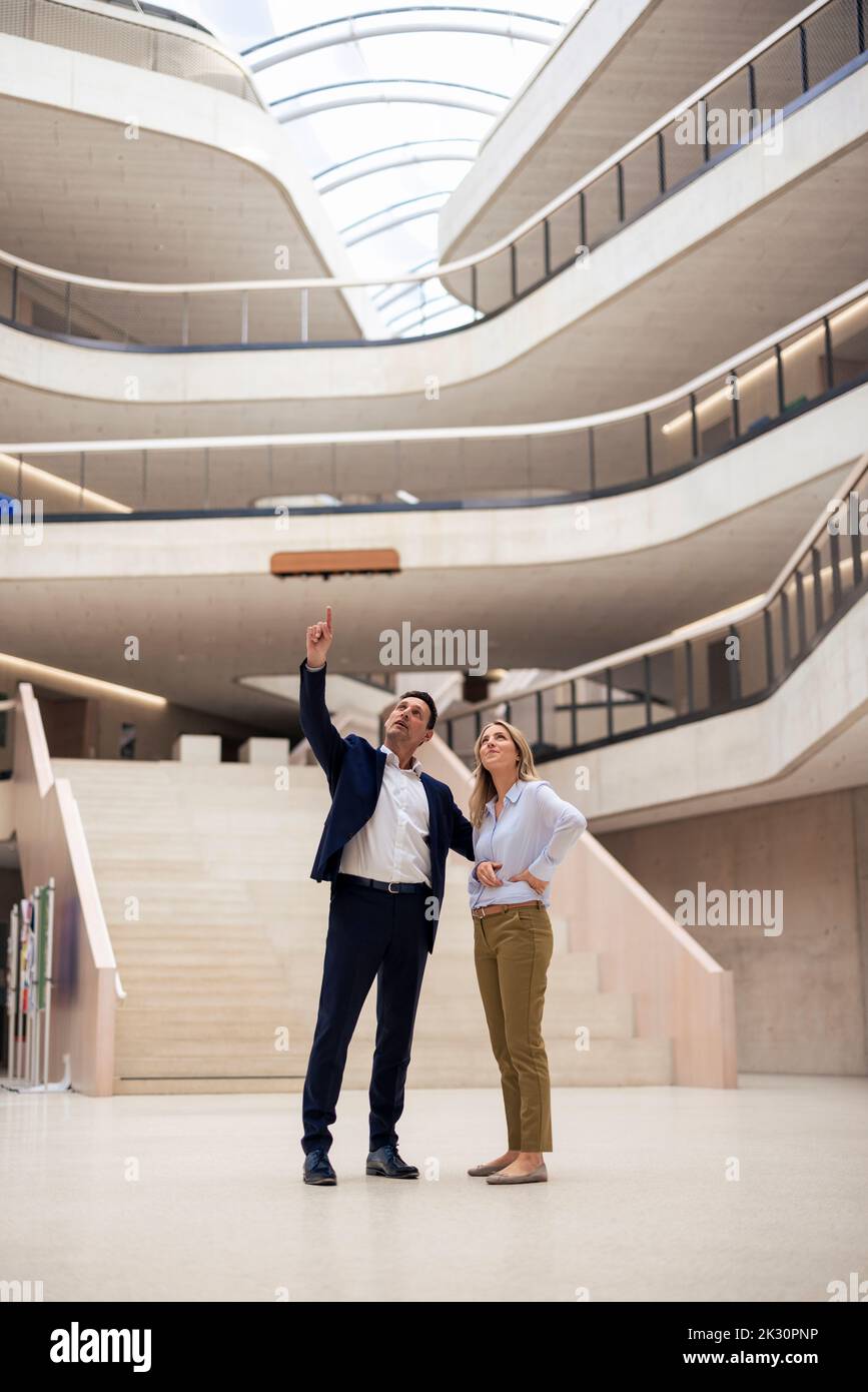 Businessman explaining colleague standing in lobby Stock Photo - Alamy