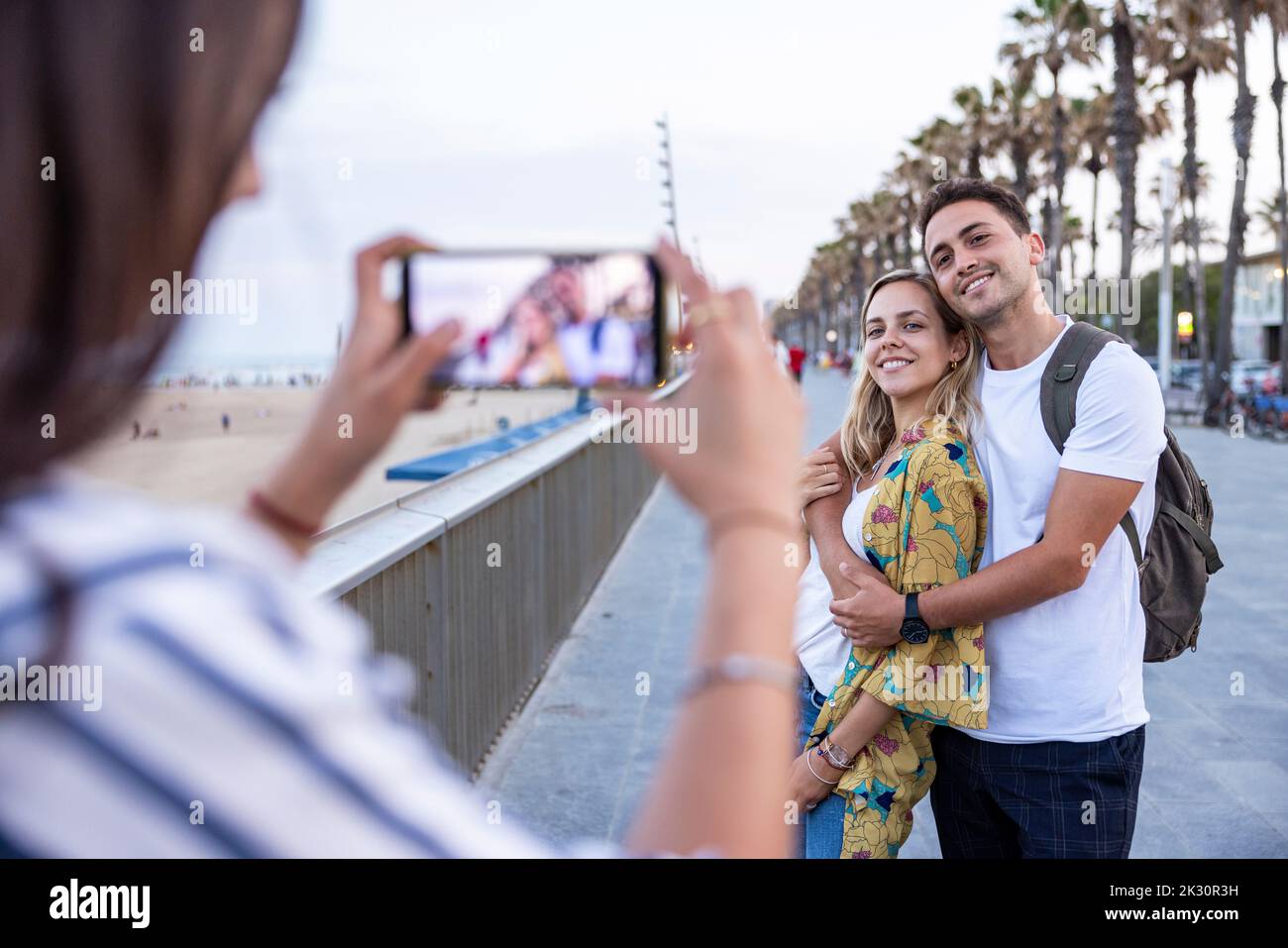Woman photographing friends through smart phone at promenade Stock ...