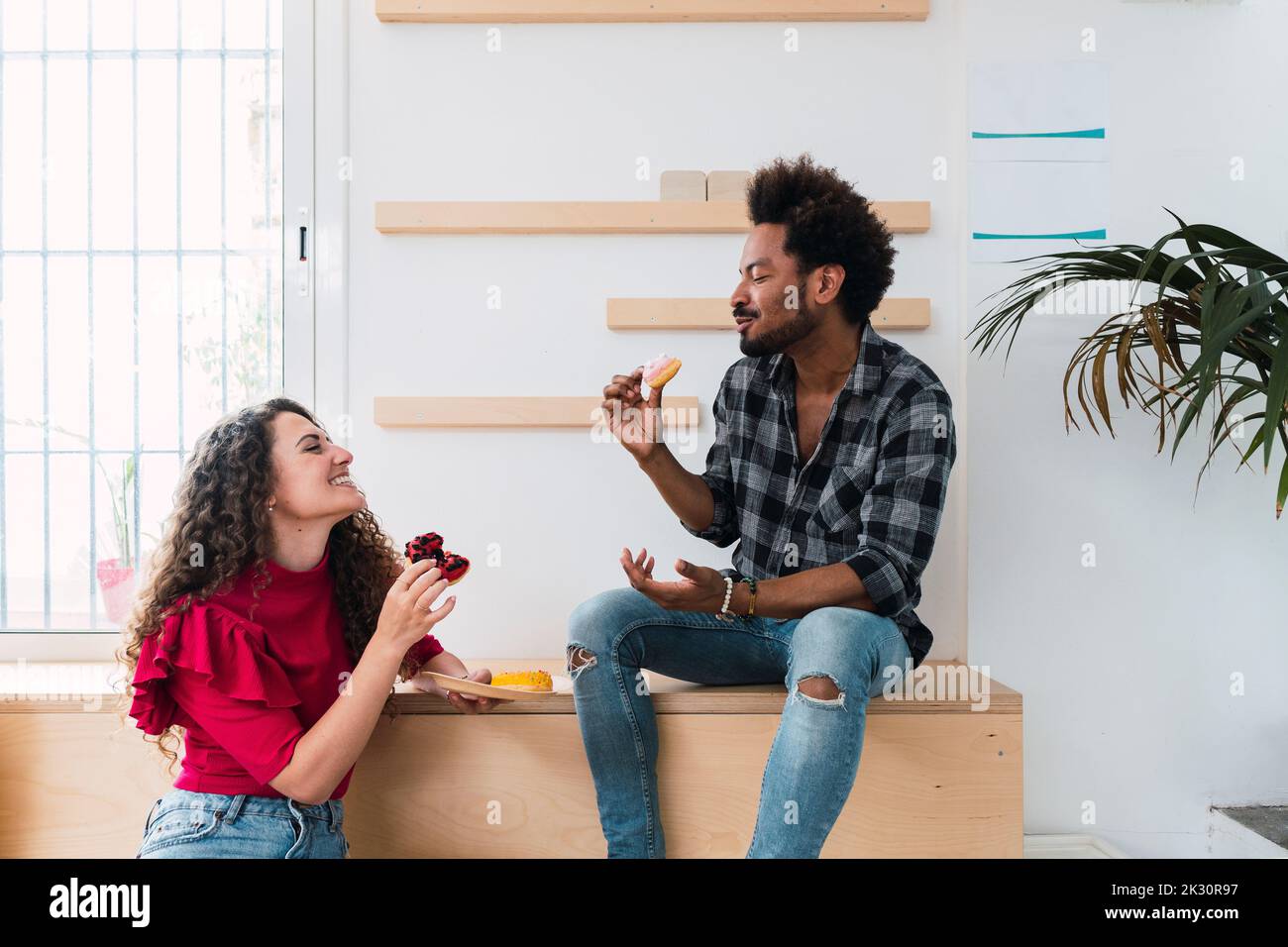 Smiling colleagues talking with each other and eating doughnuts in ...