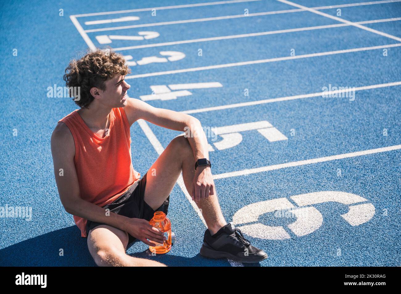 Sportsman holding water bottle sitting by starting line on track Stock ...