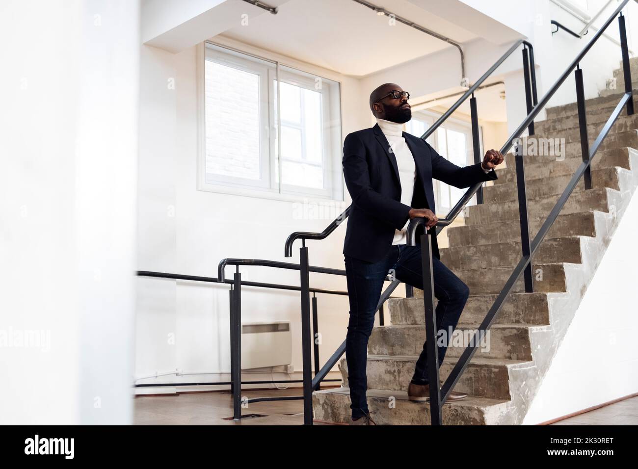 Serious businessman standing on stairs looking up Stock Photo - Alamy