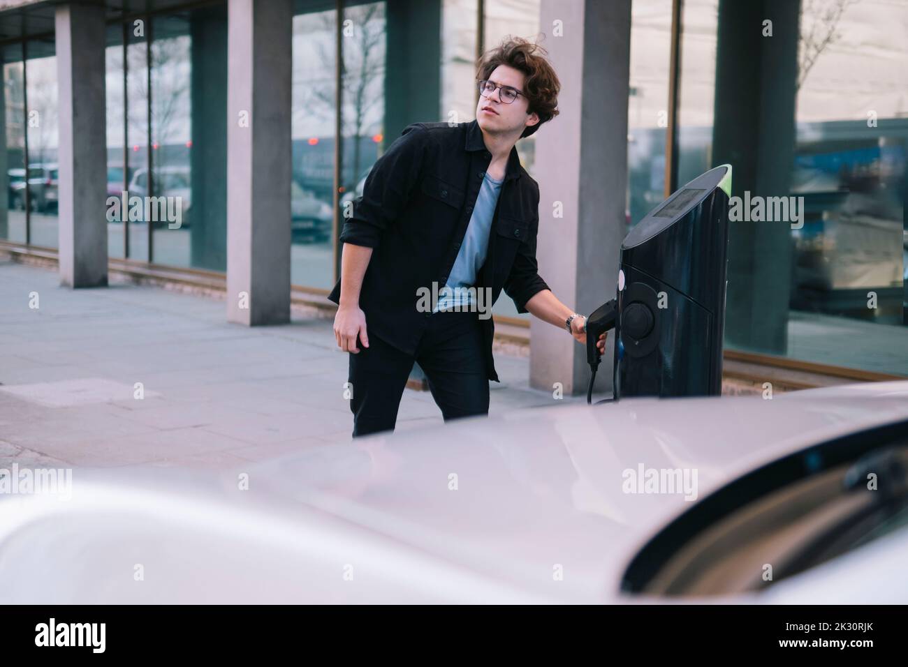 Young man pulling out electric plug at charging station Stock Photo - Alamy
