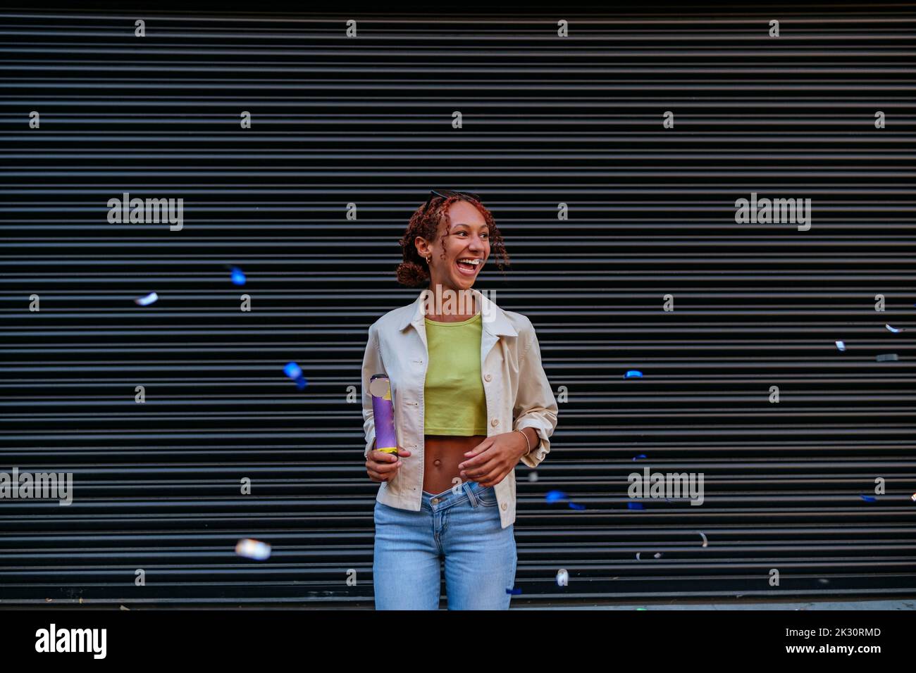Cheerful woman holding party popper in front of wall Stock Photo - Alamy