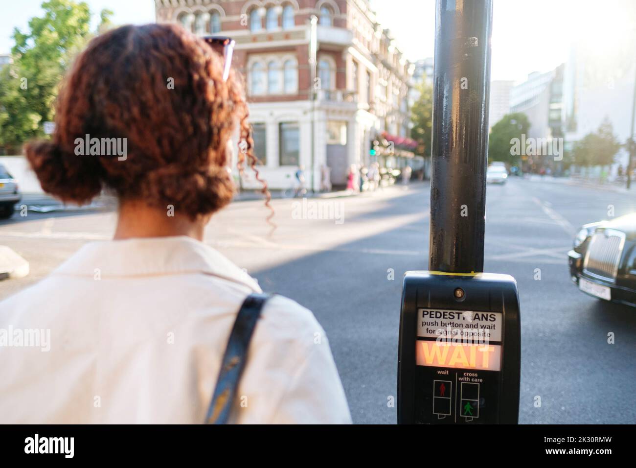 Woman waiting by pedestrian crossing button Stock Photo - Alamy