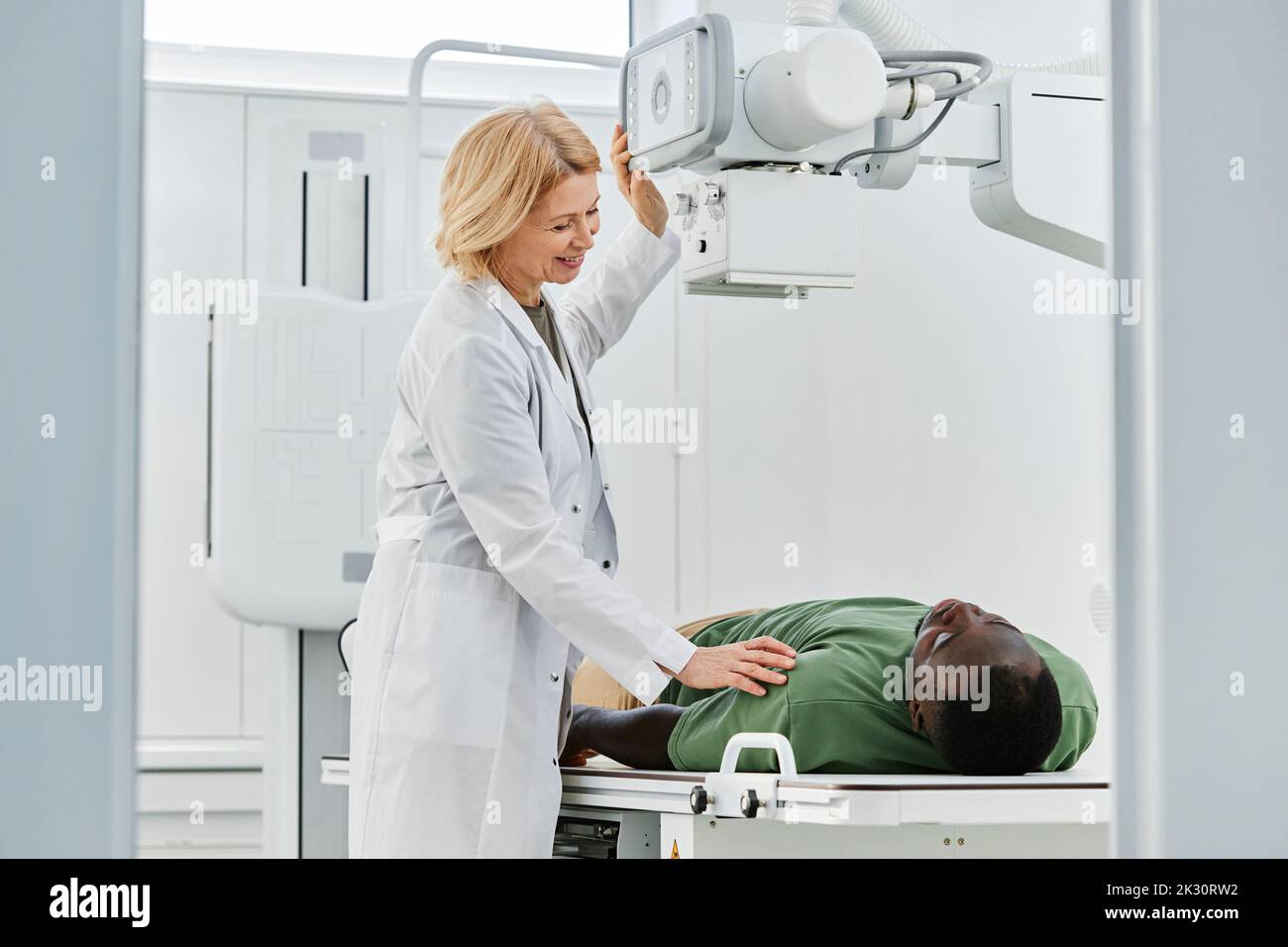 Smiling radiologist talking with patient lying on X-ray machine in ...