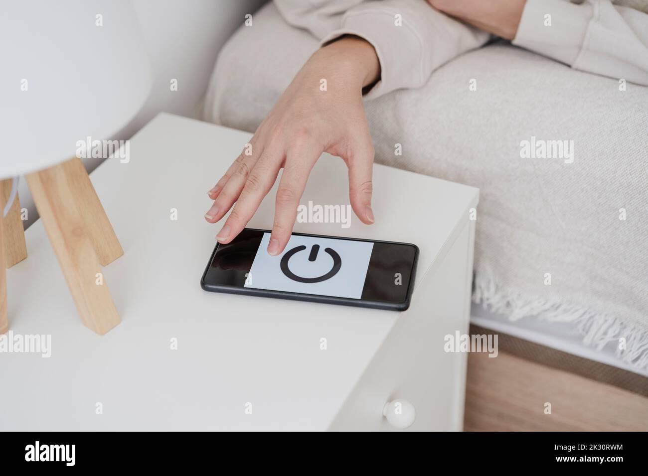 Hand of woman switching off mobile phone on night table by bed Stock ...