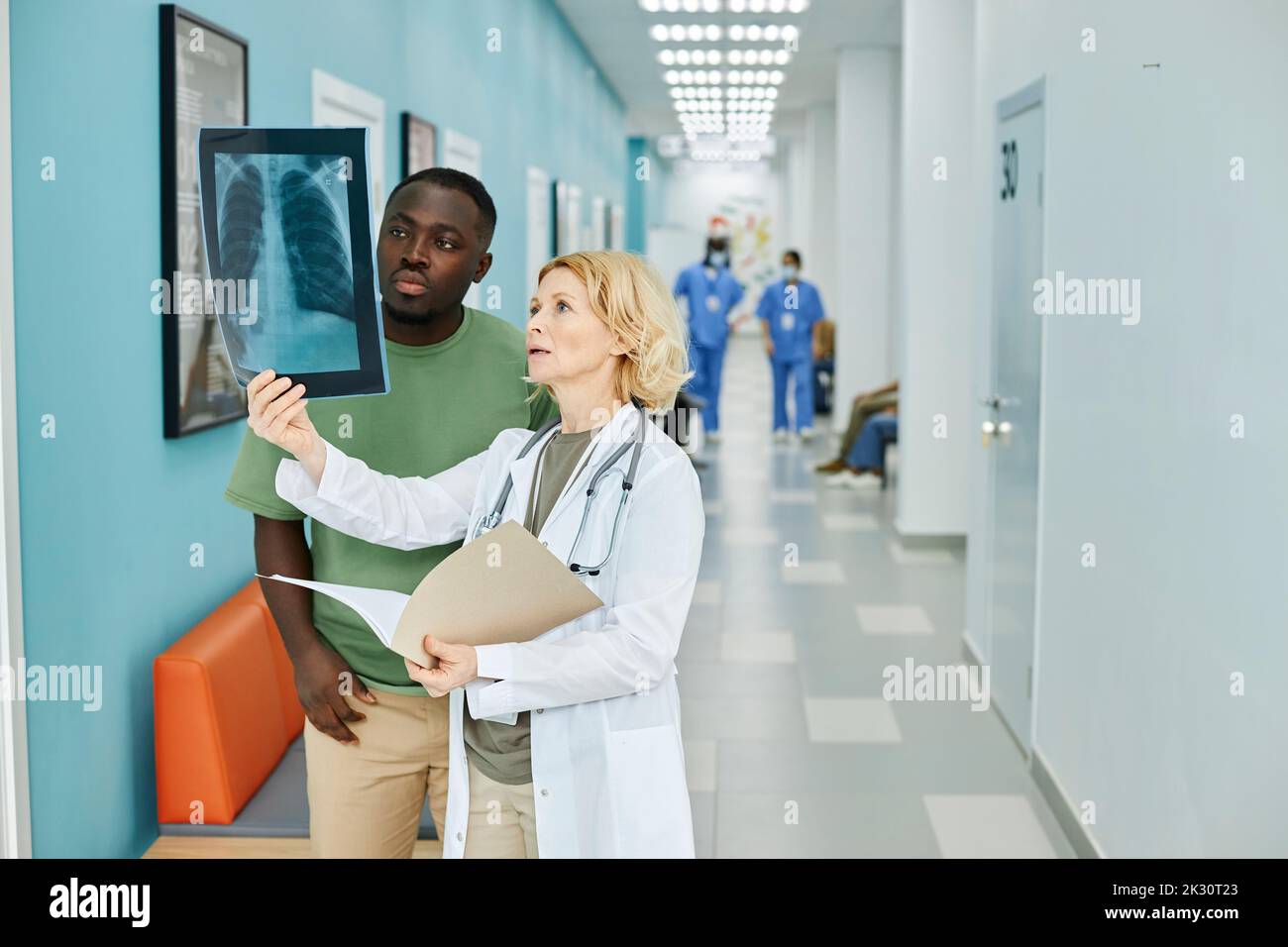 Mature doctor examining X-ray with patient standing in hospital ...