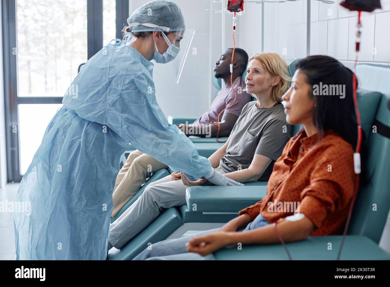 Woman donating blood talking with nurse wearing face shield in clinic ...