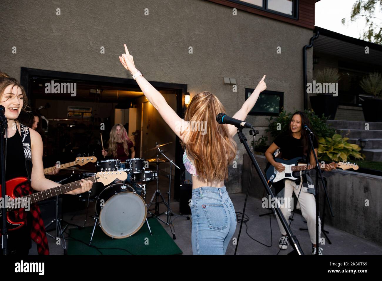 Exuberant teenage girl friends playing music as rock band in driveway ...