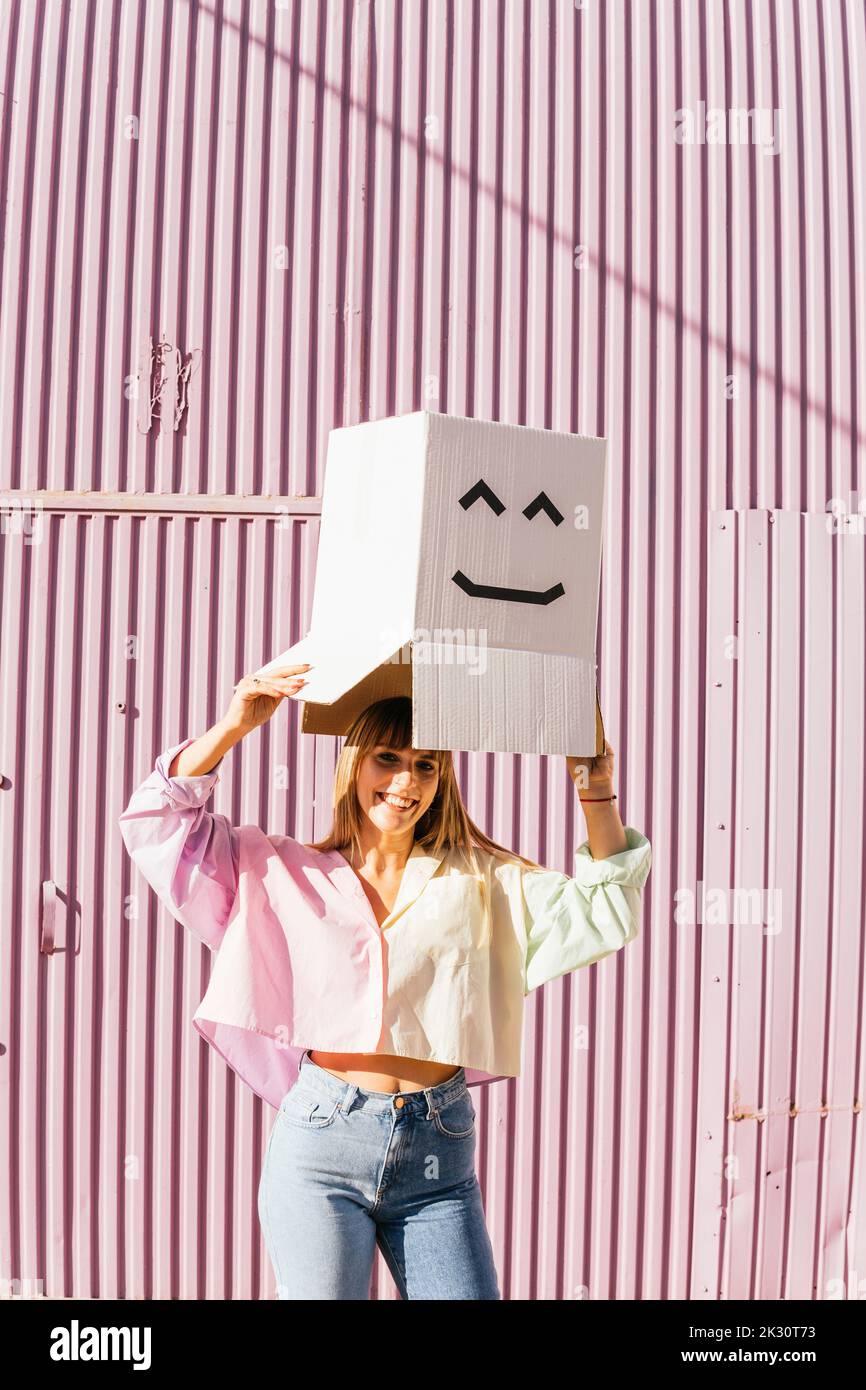 Smiling woman holding box with robot face over head in front of ...