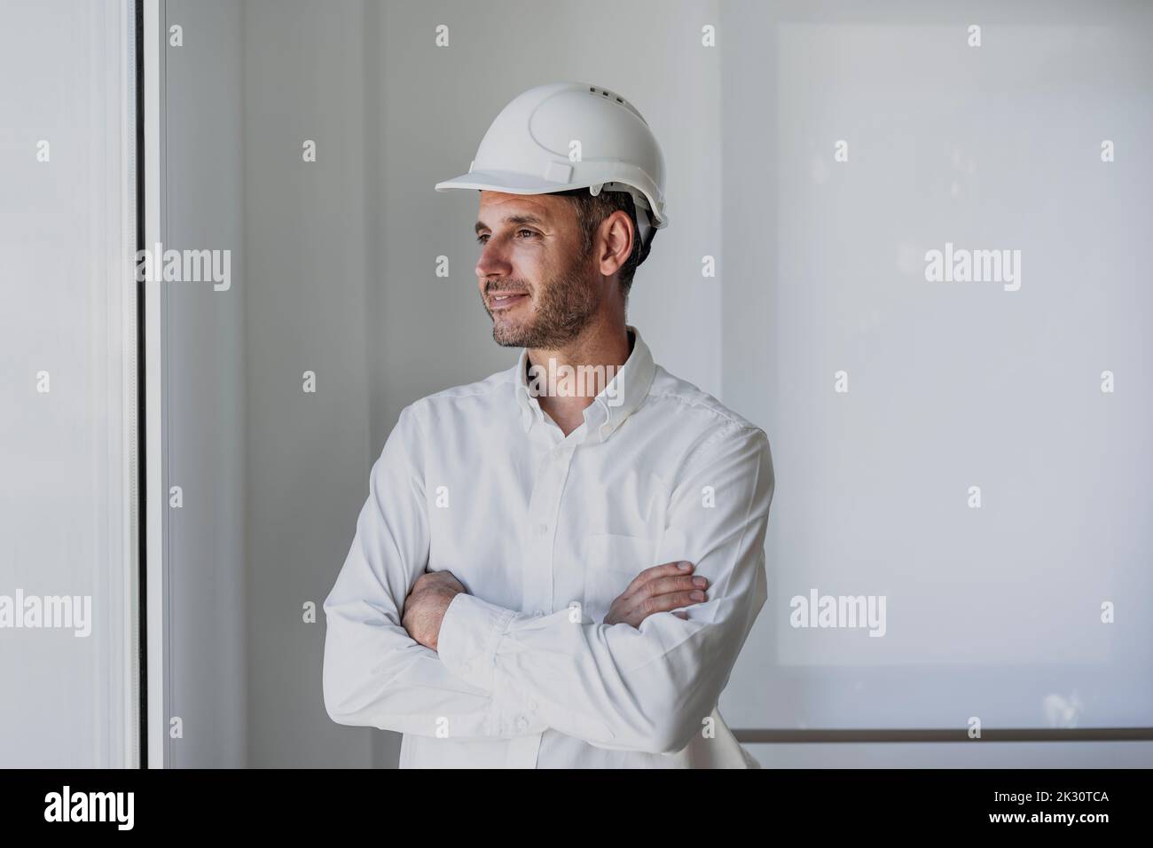 Smiling engineer with arms crossed looking through window in front of ...