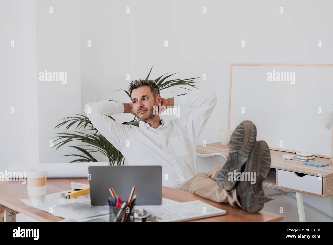 Smiling businessman with hands behind head resting on chair in office ...