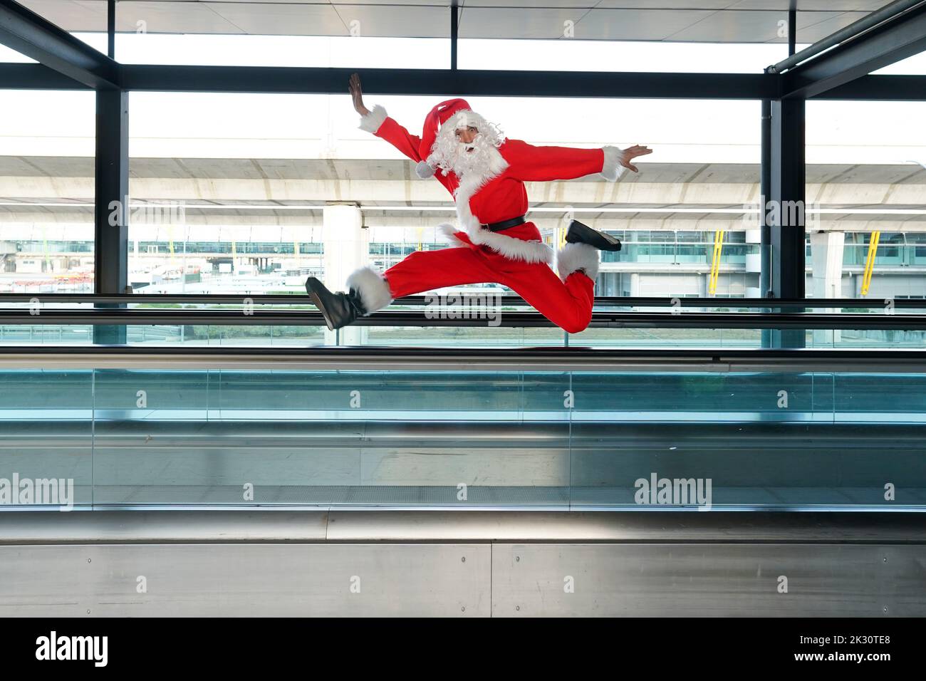 Man wearing Santa Claus costume jumping on moving walkway at airport ...