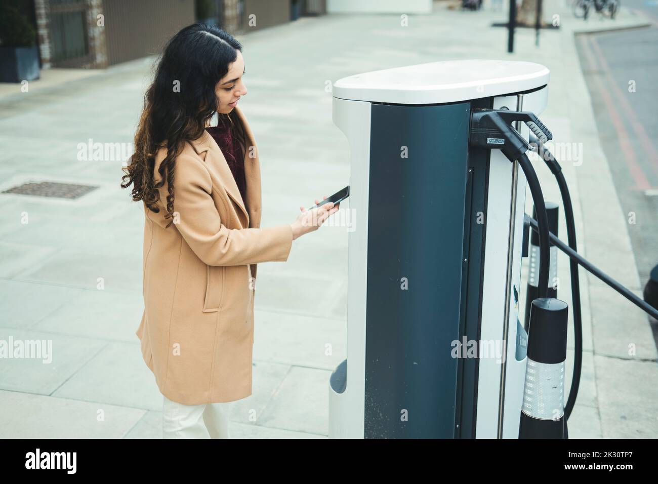 Young woman with smart phone making contactless payment at electric ...