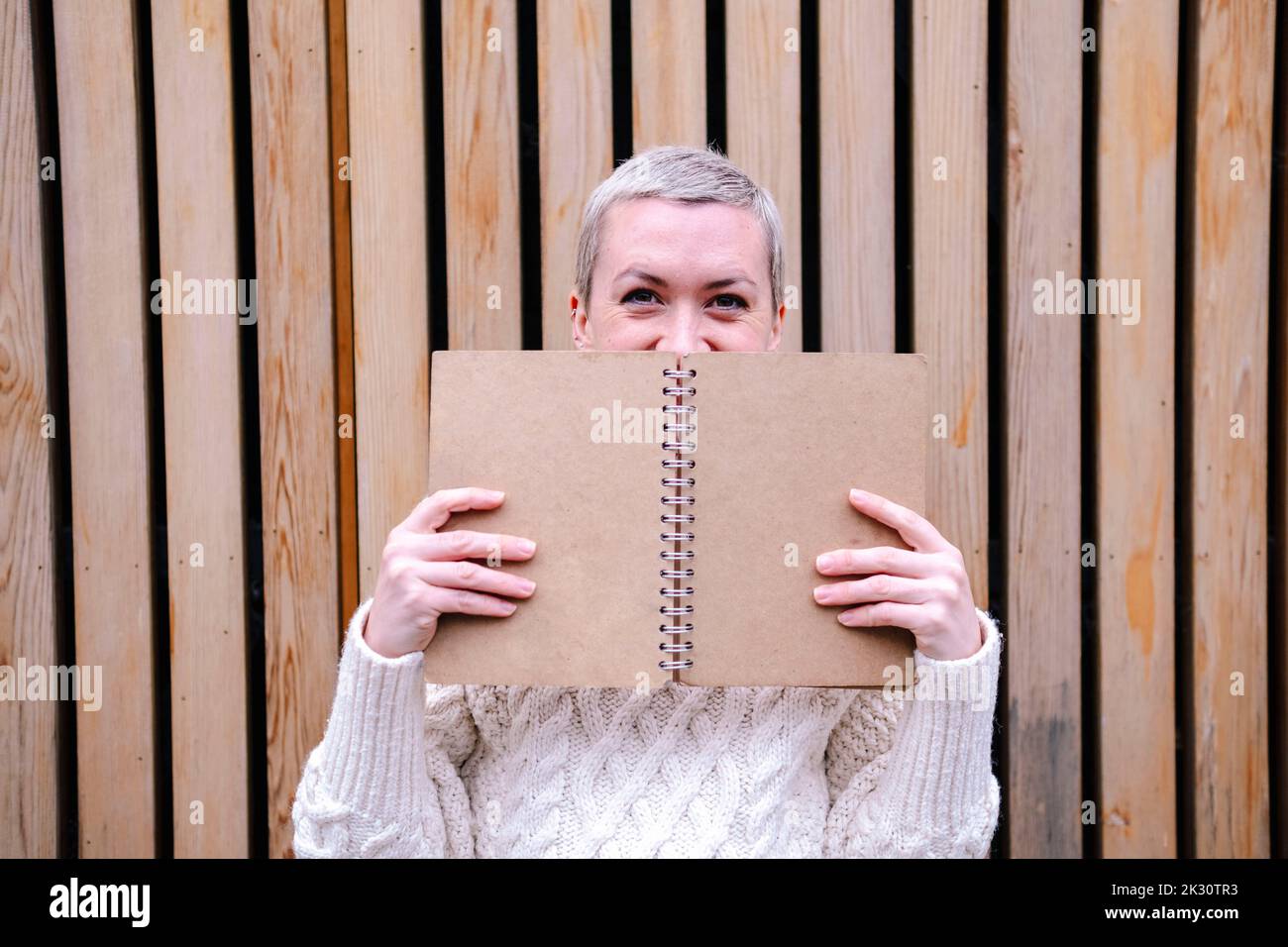 Woman hiding face behind open book in front of wall Stock Photo - Alamy