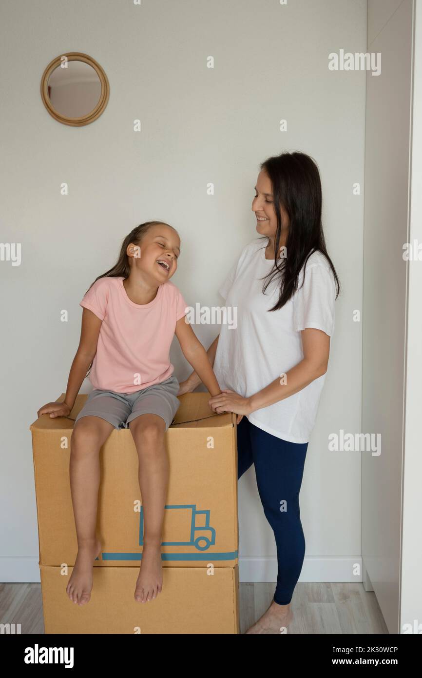 Mother looking at happy daughter sitting on box Stock Photo - Alamy
