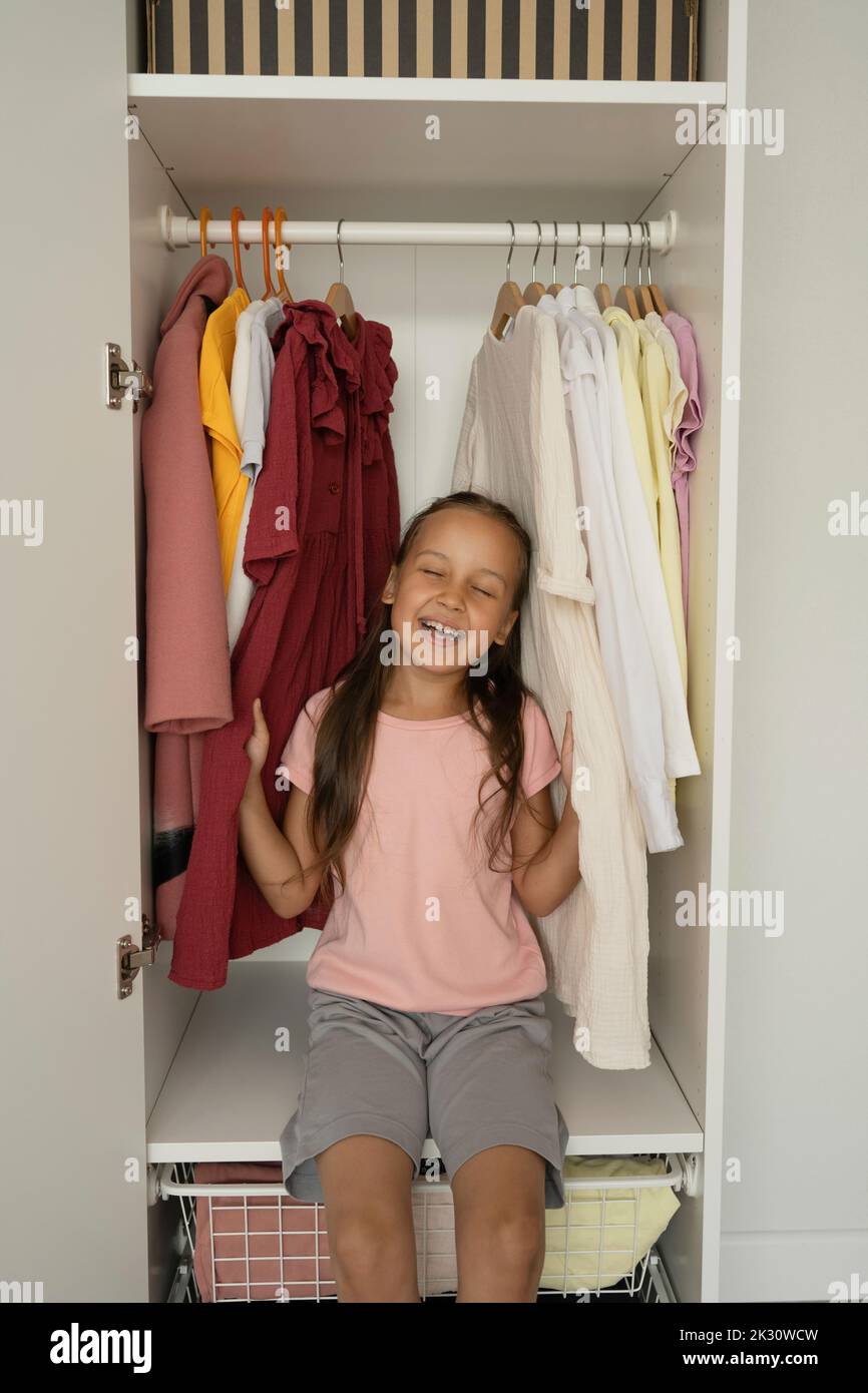 Happy girl with eyes closed sitting by clothes in closet Stock Photo ...