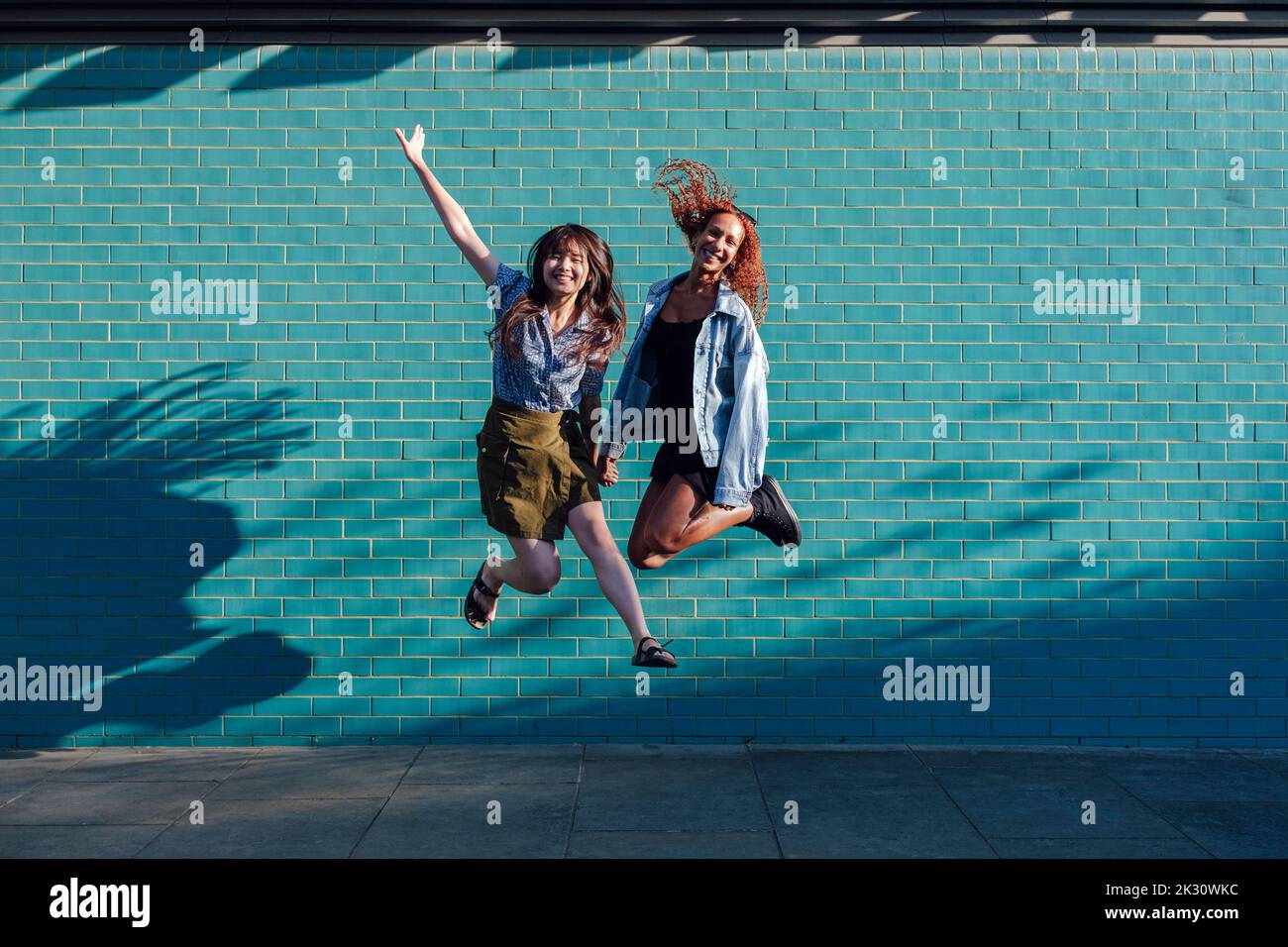 Happy young friends jumping together in front of wall Stock Photo - Alamy