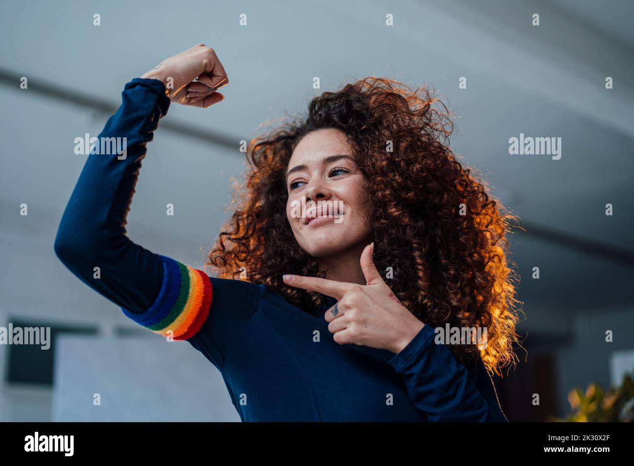 Smiling young woman flexing muscles pointing at rainbow arm band Stock ...