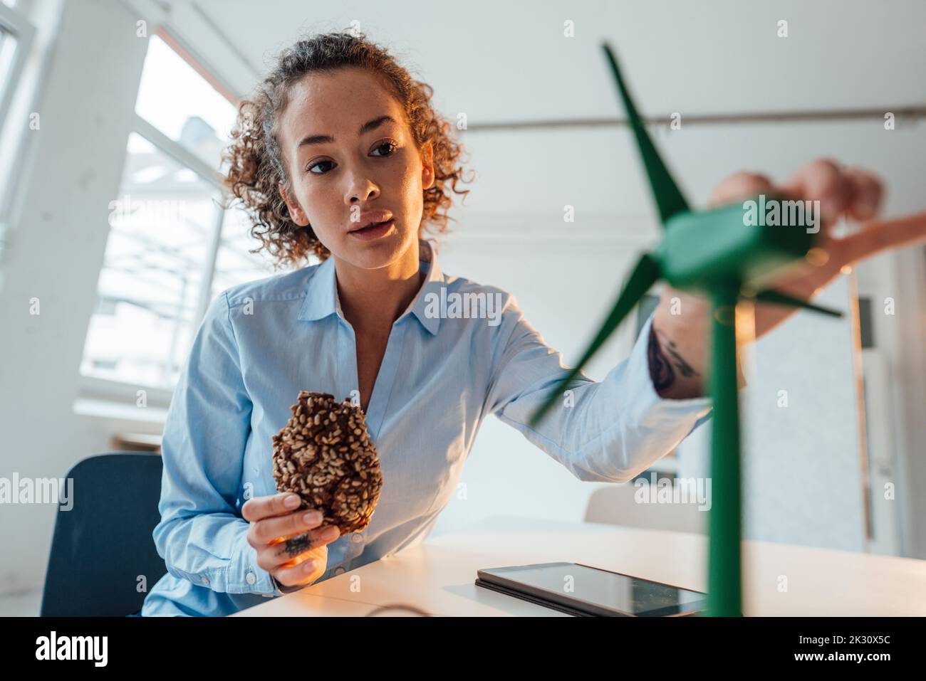 Young engineer holding cookie examining wind turbine model at desk in ...