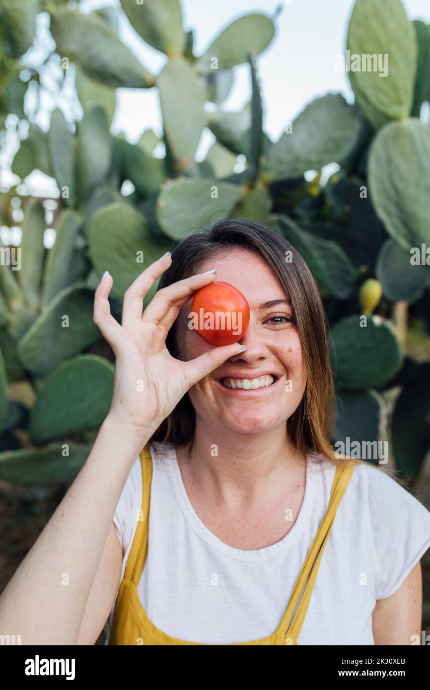 Smiling young farm worker covering eye with tomato Stock Photo - Alamy
